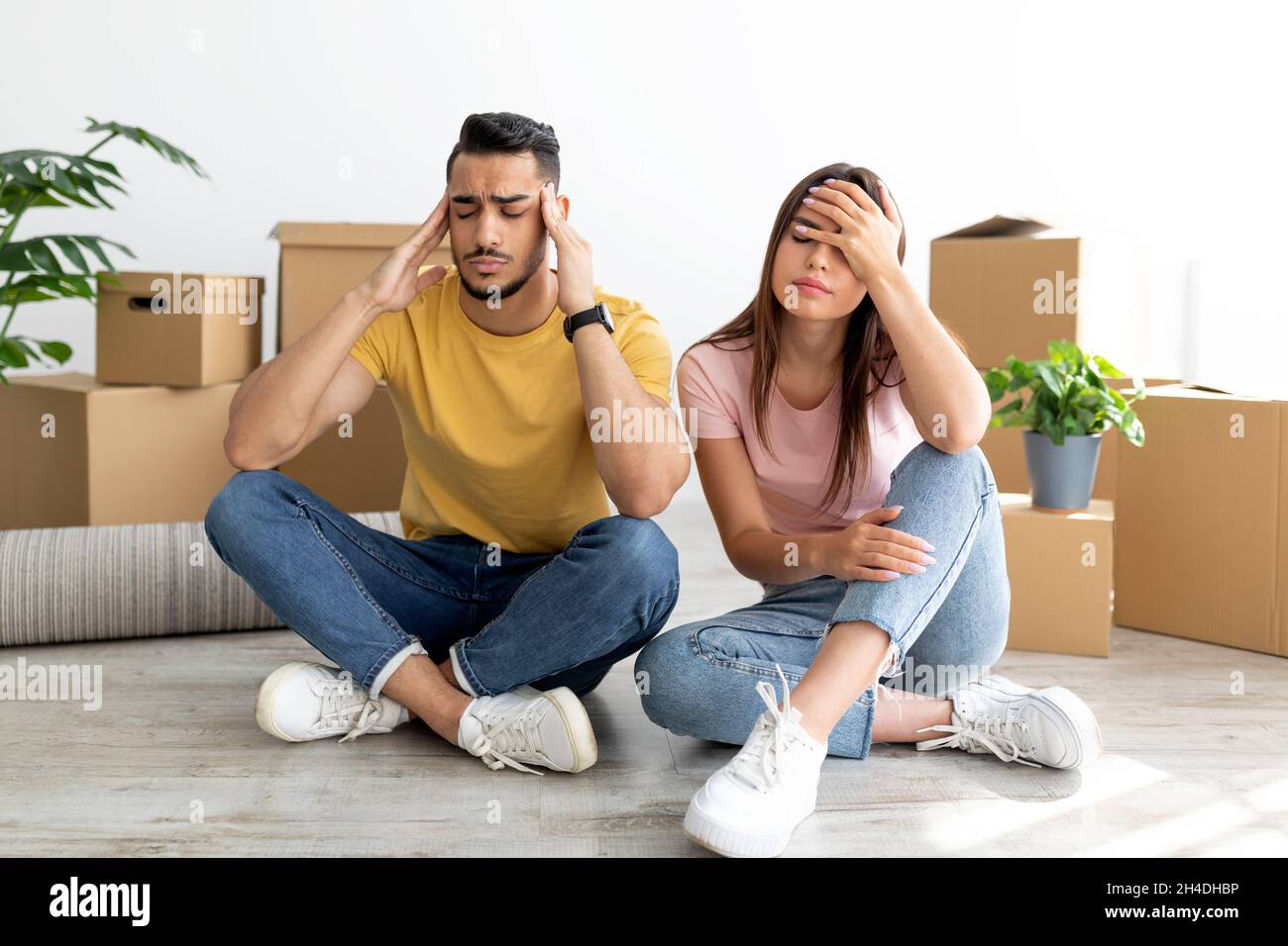 Tired young multiracial couple sitting on floor among boxes, massaging ...
