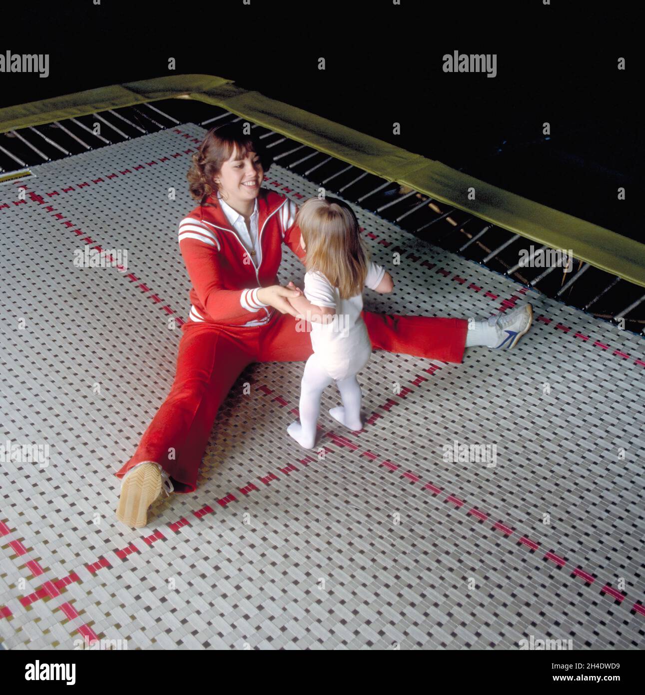 A gymnastics instructor gives lessons to a toddler on a trampoline in ...