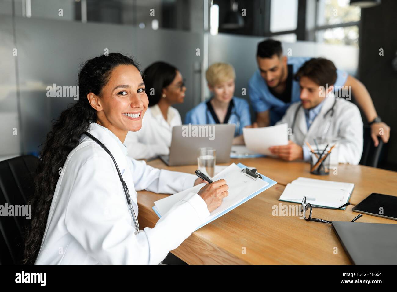 Female doc smiling at camera while having brainstorming with colleagues ...