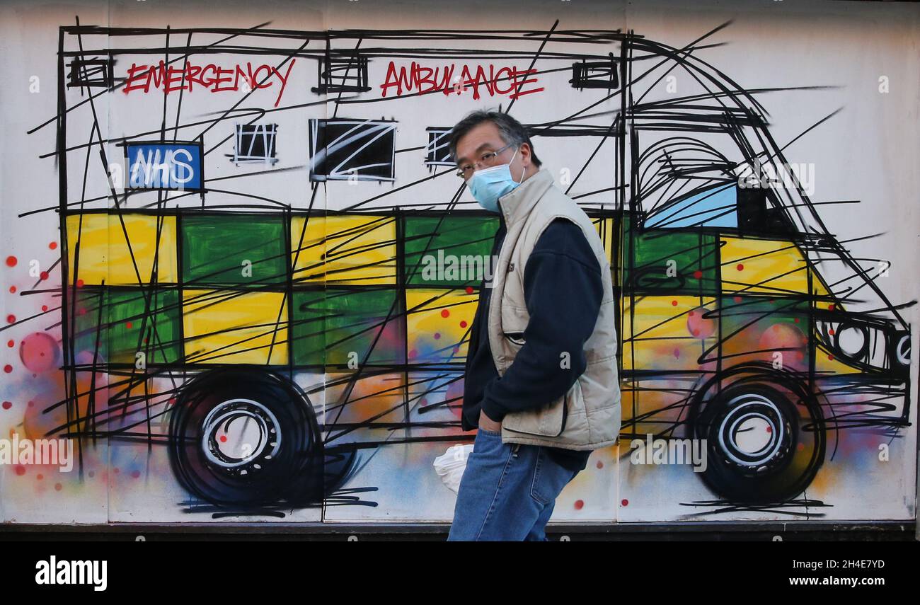 A man wearing a surgical face mask walks past a graffiti in tribute to ...