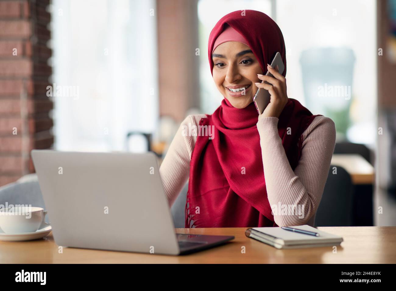 Beautiful muslim woman working online, having phone conversation, using ...