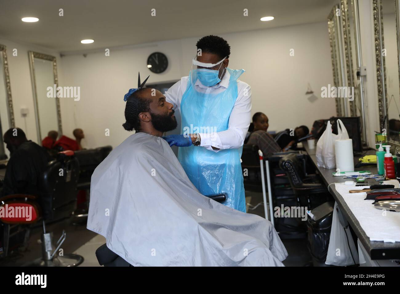 A barber wearing Personal Protective Equipment (PPE) gives a cut hair ...