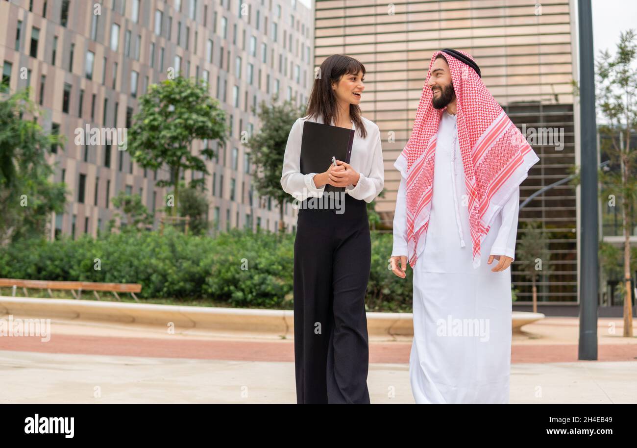 Low angle of friendly businesswoman smiling and speaking with Arab male ...