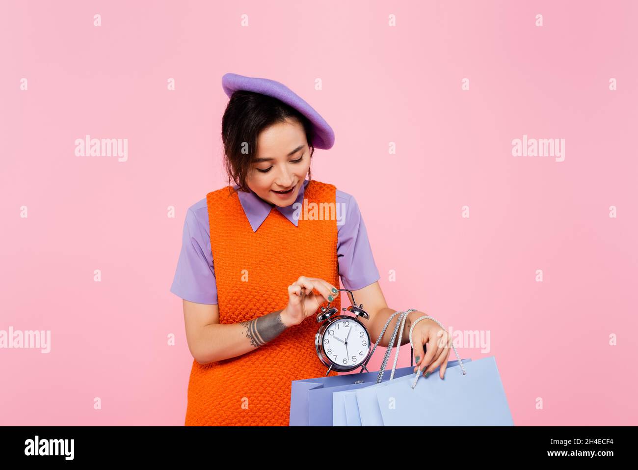 trendy woman in orange sleeveless dress putting vintage alarm clock ...
