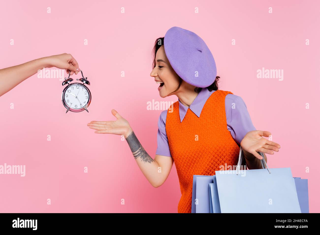 amazed woman showing wow gesture near female hand with vintage alarm ...