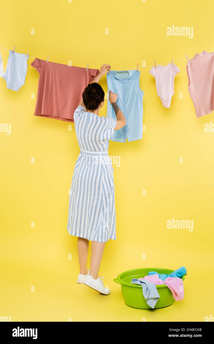 back view of housewife hanging clothes on rope on yellow background ...