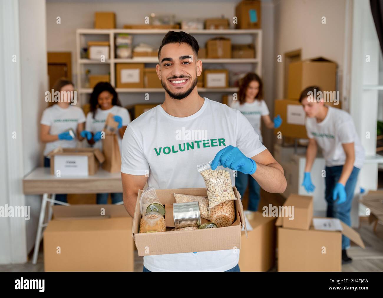 Young arab volunteer working at charity center, holding food donation ...