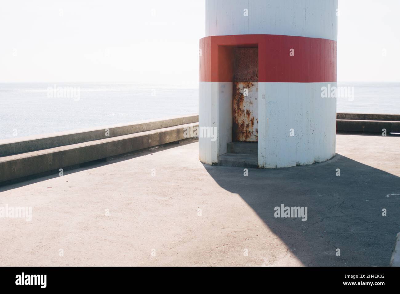 Red and white striped lighthouse with a rusty door on a pier Stock ...