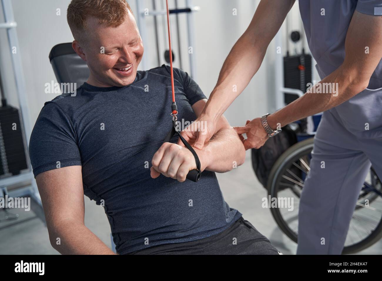 Trainer assist happy man with disability who lift weight on simulator ...
