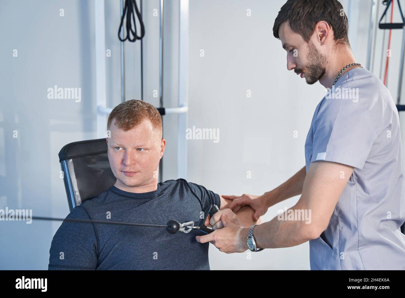 Doctor aid handicapped man pull hand on rehabilitation weight machine ...