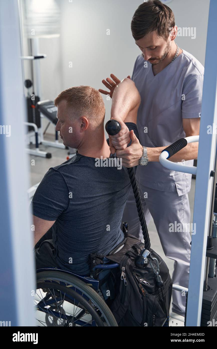 Doctor helps wheelchair man pull strength tether with hand back view ...