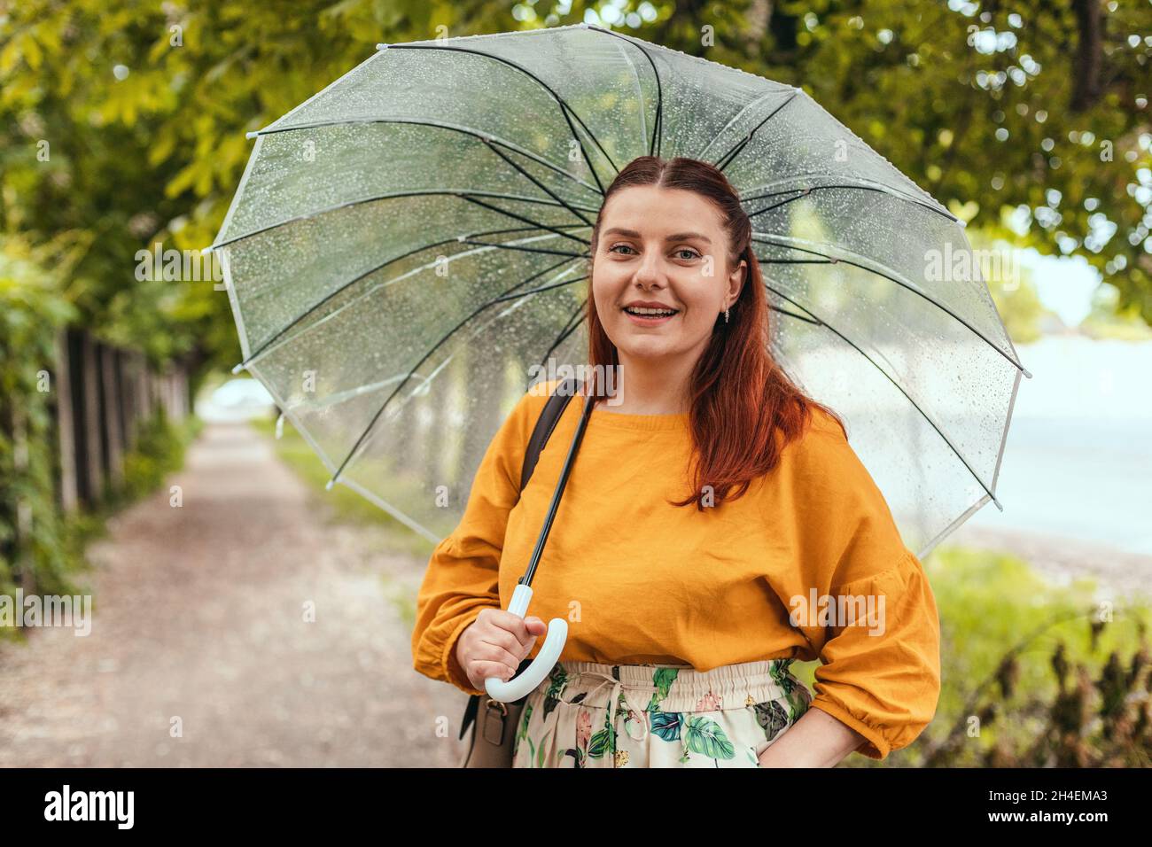 Stylish young woman in bright clothes under a transparent umbrella in ...