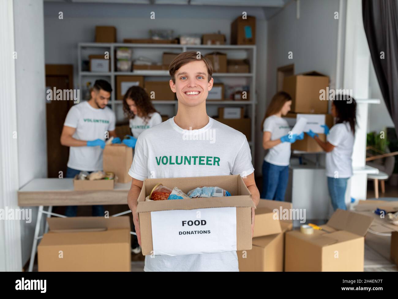 Happy young male volunteer in uniform holding box for donation, team ...