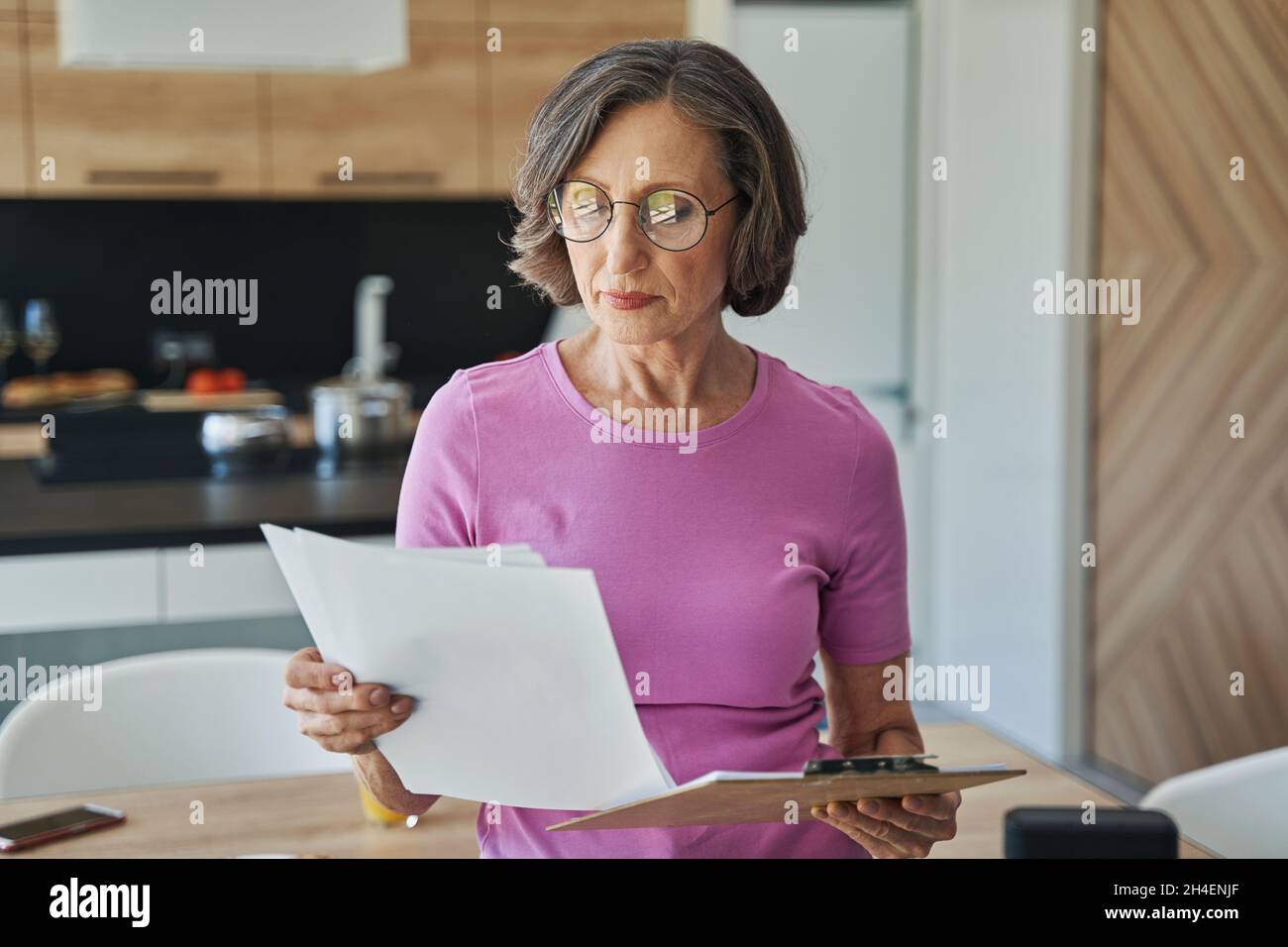 Senior lady looking through document in kitchen Stock Photo - Alamy