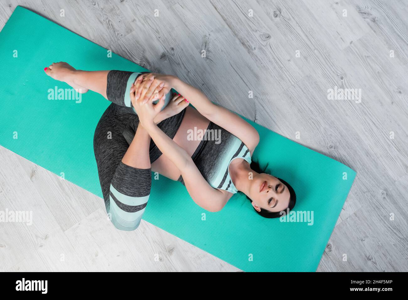 top view of pregnant woman meditating in wind removing pose on yoga mat ...