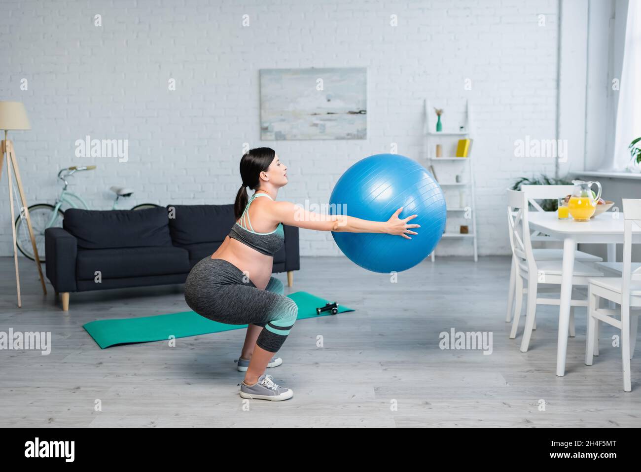 side view of pregnant woman doing sit ups with fitness ball near table ...