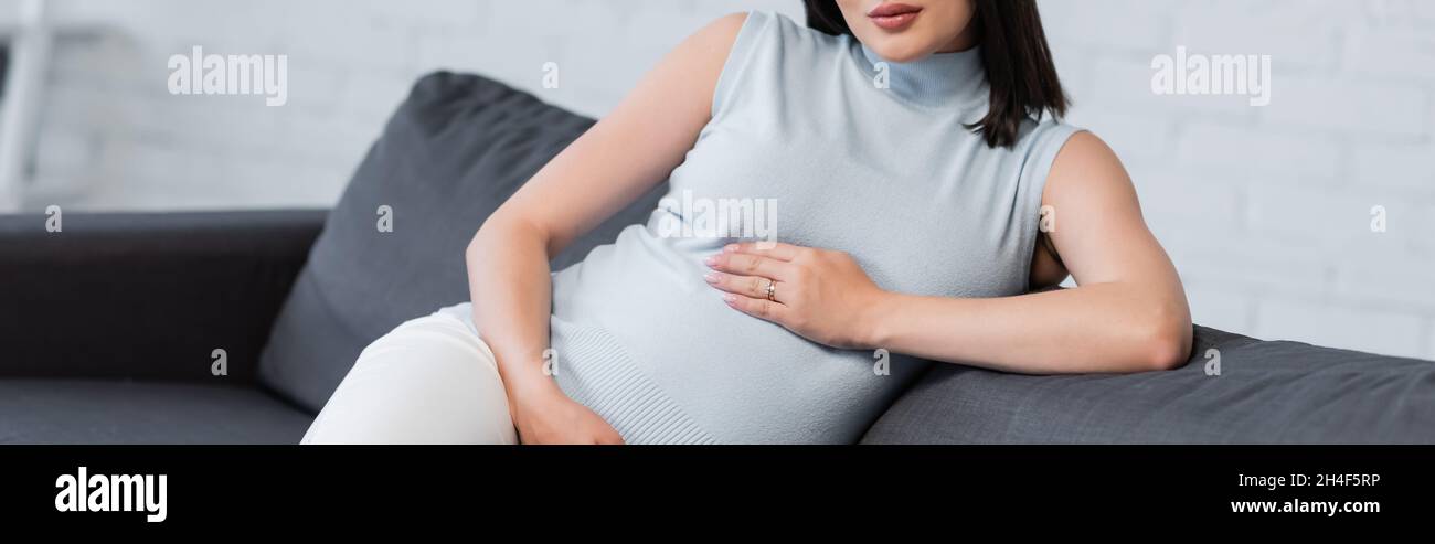 cropped view of pregnant woman touching belly while sitting on couch at ...