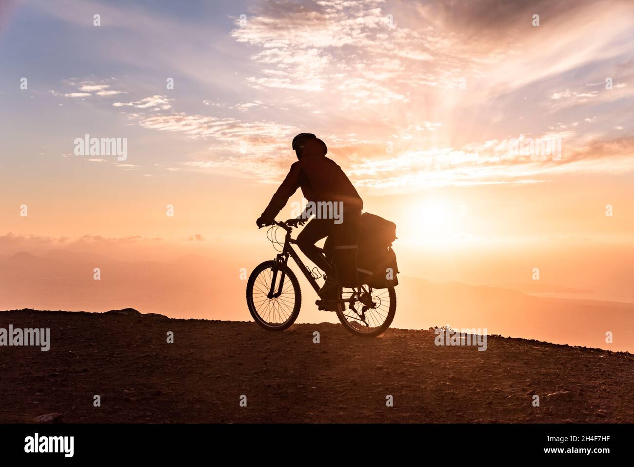 Mountain bicycle rider with backpack travels over sunrise background ...