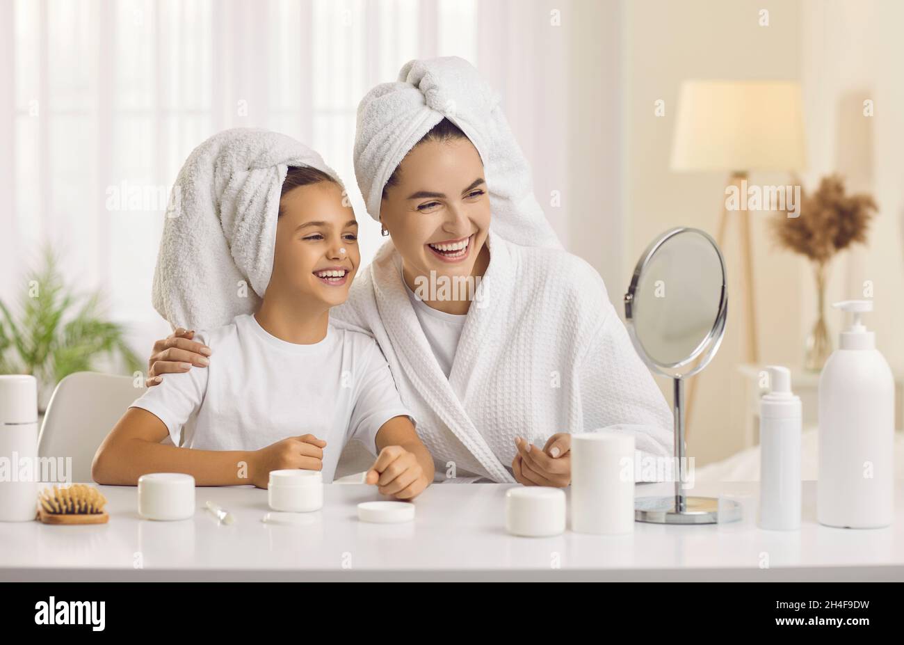 Happy Mother And Her Daughter Applying Face Cream Looking In Mirror