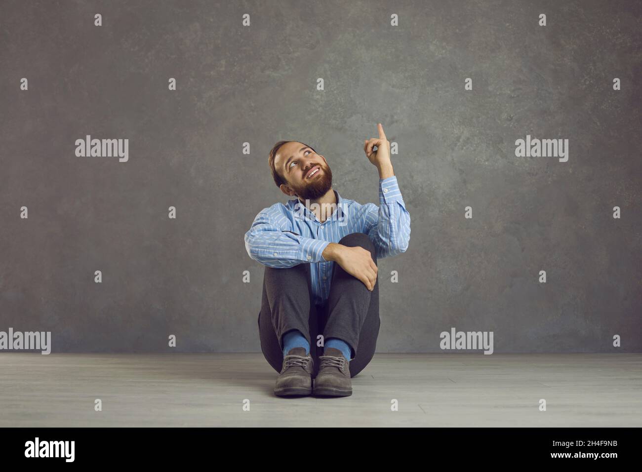 Funny caucasian man thinking sitting with raised finger on the floor on ...
