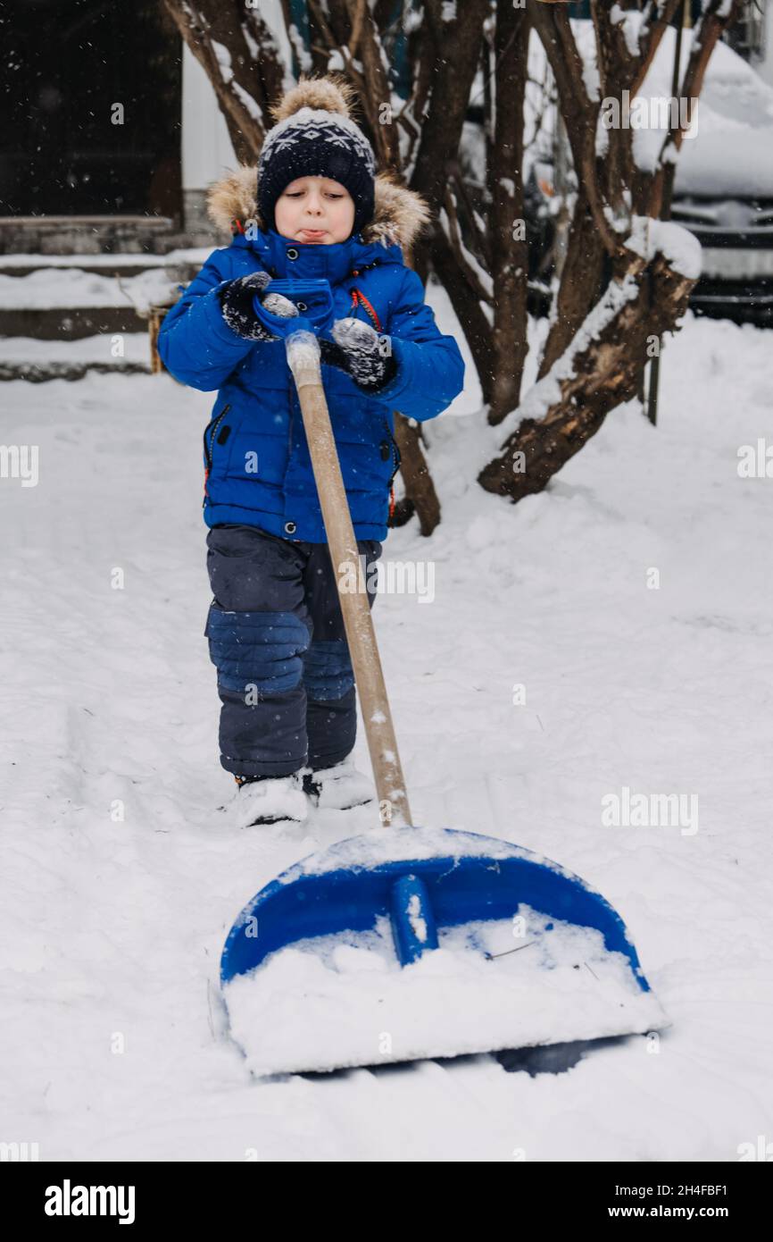 Little boy with a shovel in hand remove snow in backyard, snow removal ...