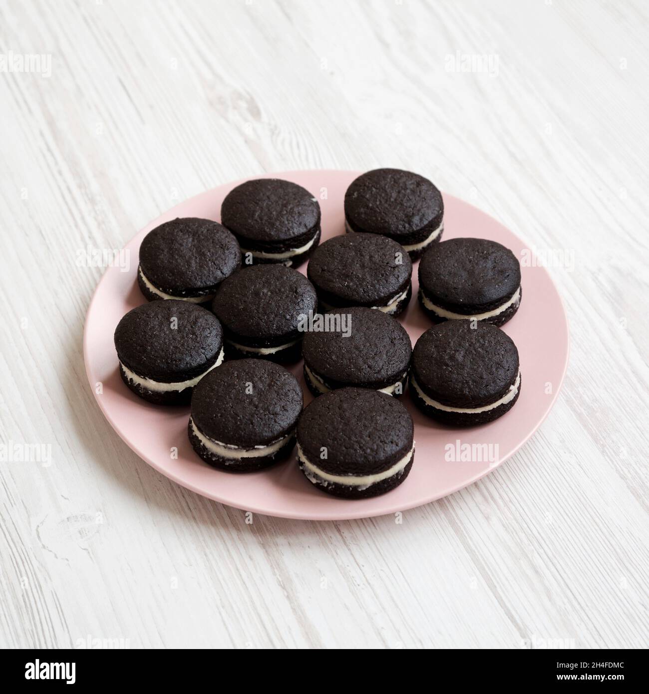 Homemade Oreos on a pink plate on a white wooden background, side view ...