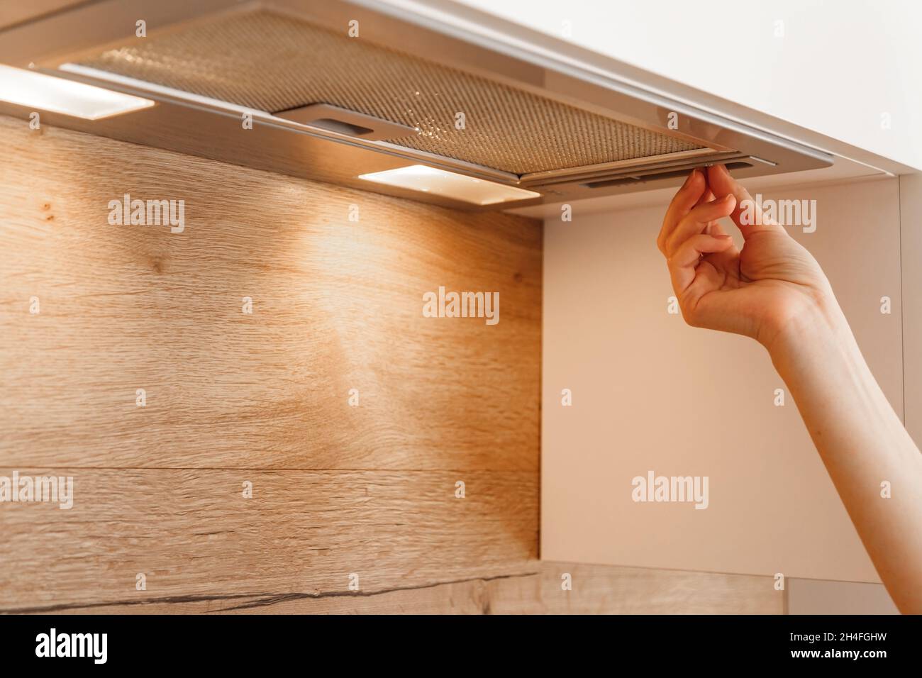 Woman hand turn on embedded cooker hood in white modern kitchen ...