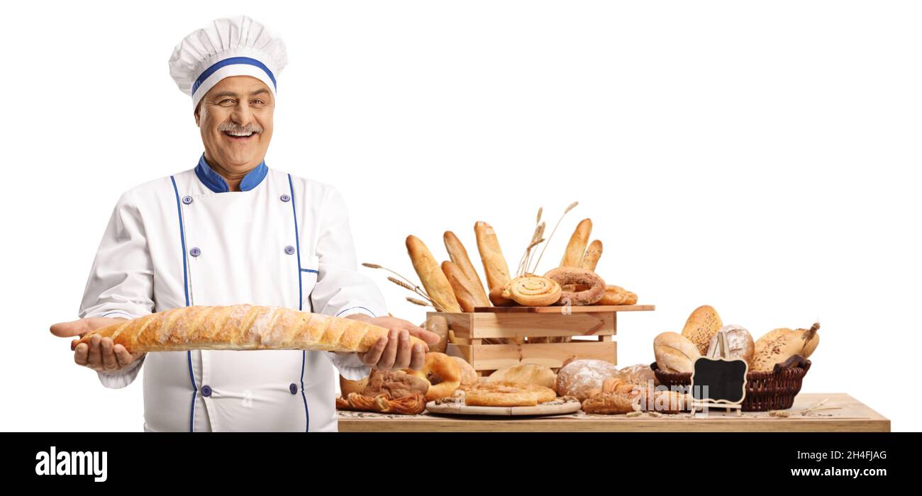 Mature male chef holding a baguette bread in front of a table with different breads isolated on ...
