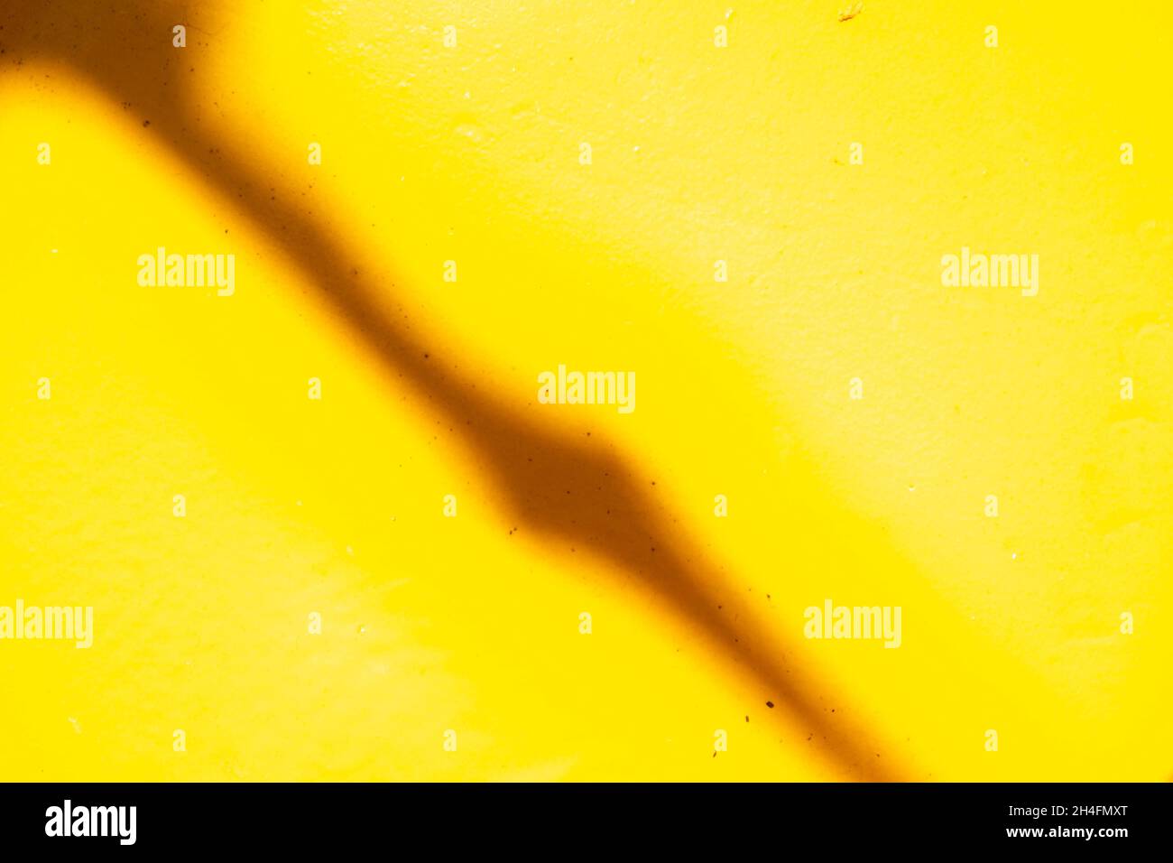 A diagonal thin shadow on the old faded yellow paint which is covered ...