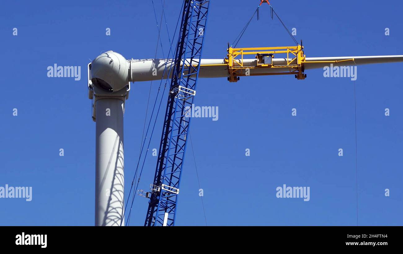 Distant view of a crane erecting a wind turbine blade with a blue sky ...