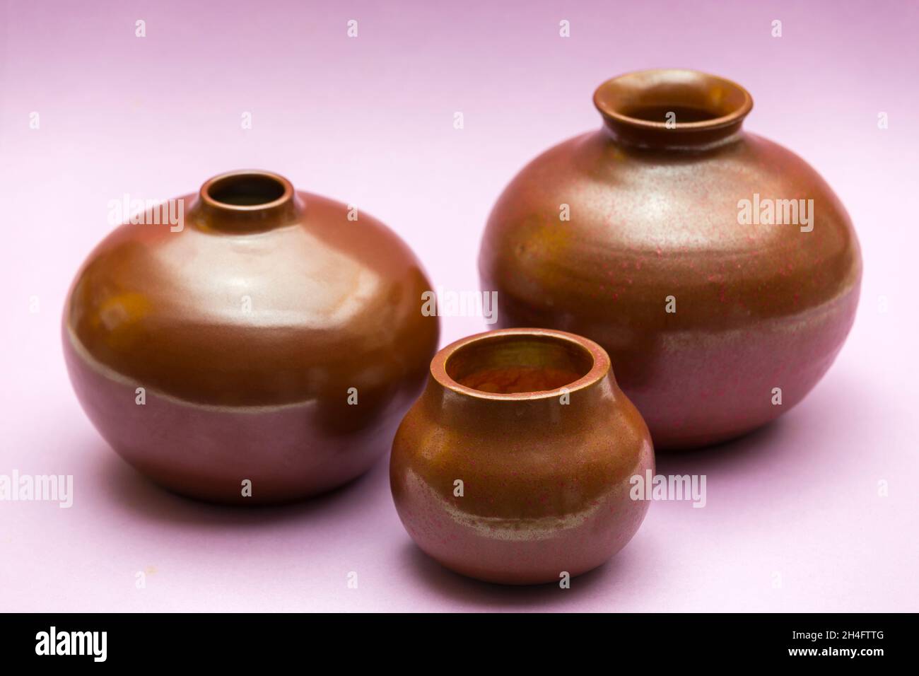 still life with three ceramic pots, in brown tones, placed on a pink ...