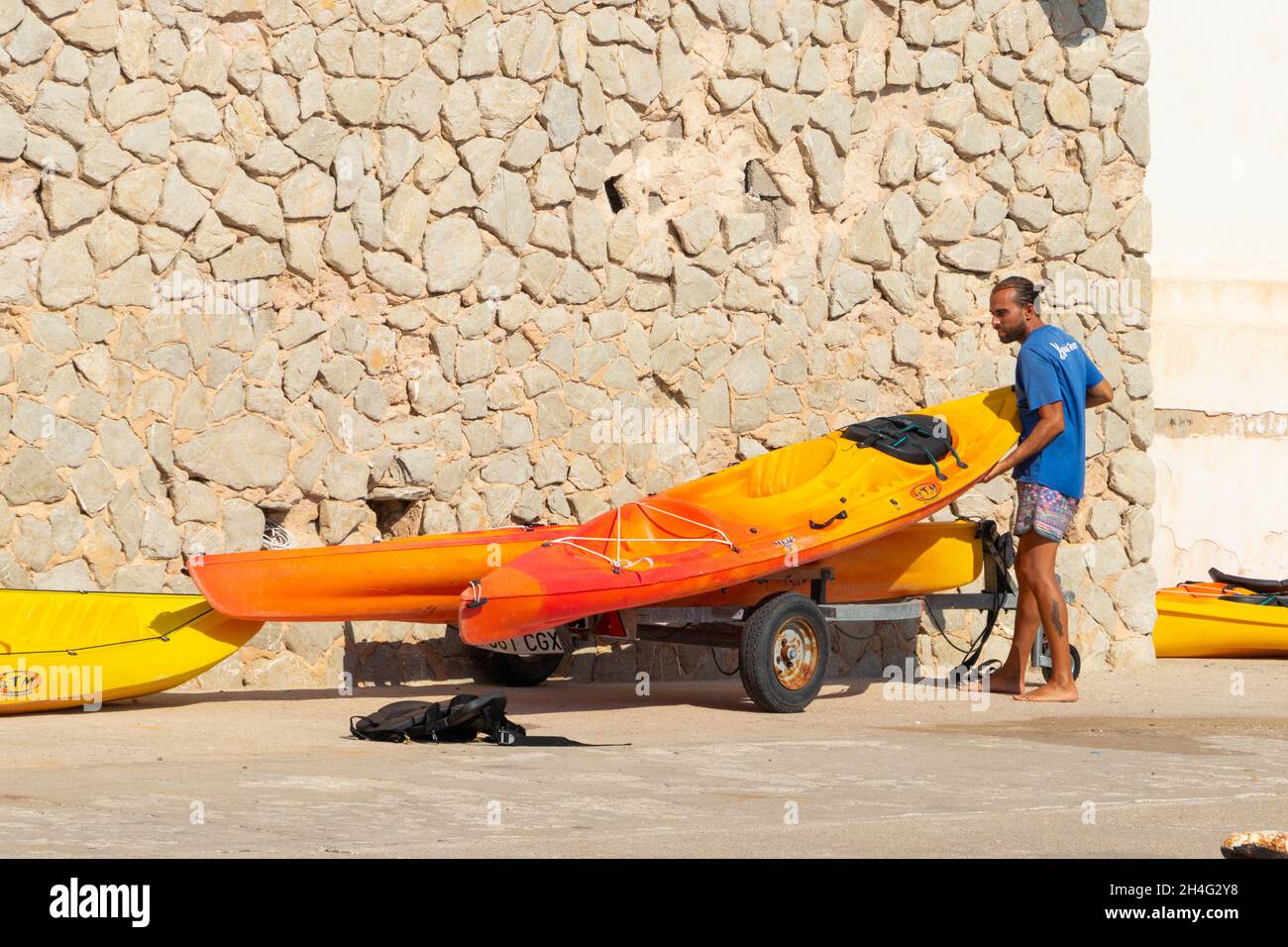 Spanish man in shorts unloading canoes in harbour in Sant Elm Mallorca ...