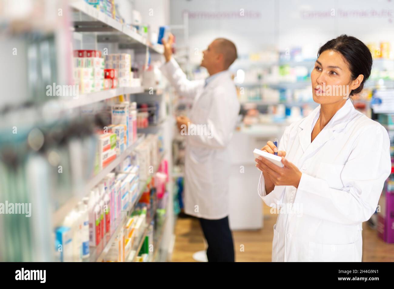 Positive female pharmacist makes notes on a notebook in the sales area ...