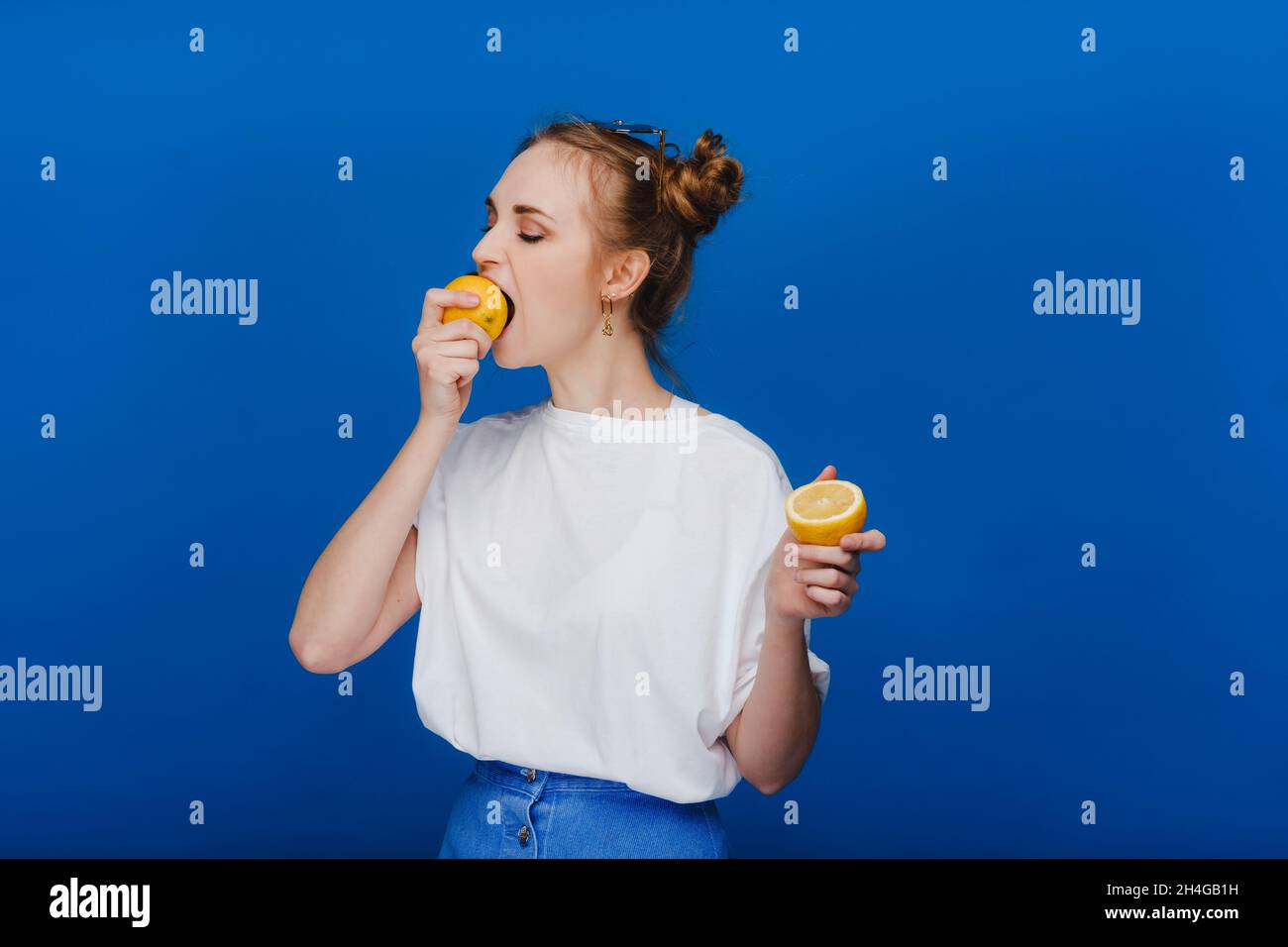 Beautiful brunette woman takes a bite of a lemon. Girl on a blue ...