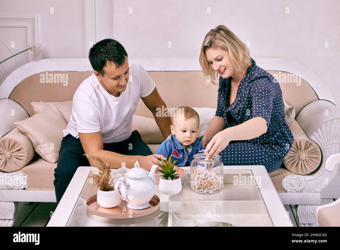 Toddler with parents sit on couch in lounge Stock Photo - Alamy