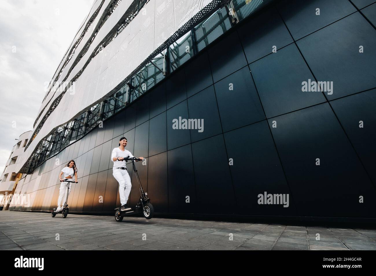 A girl and a guy are walking on electric scooters around the city, a couple in love on scooters ...