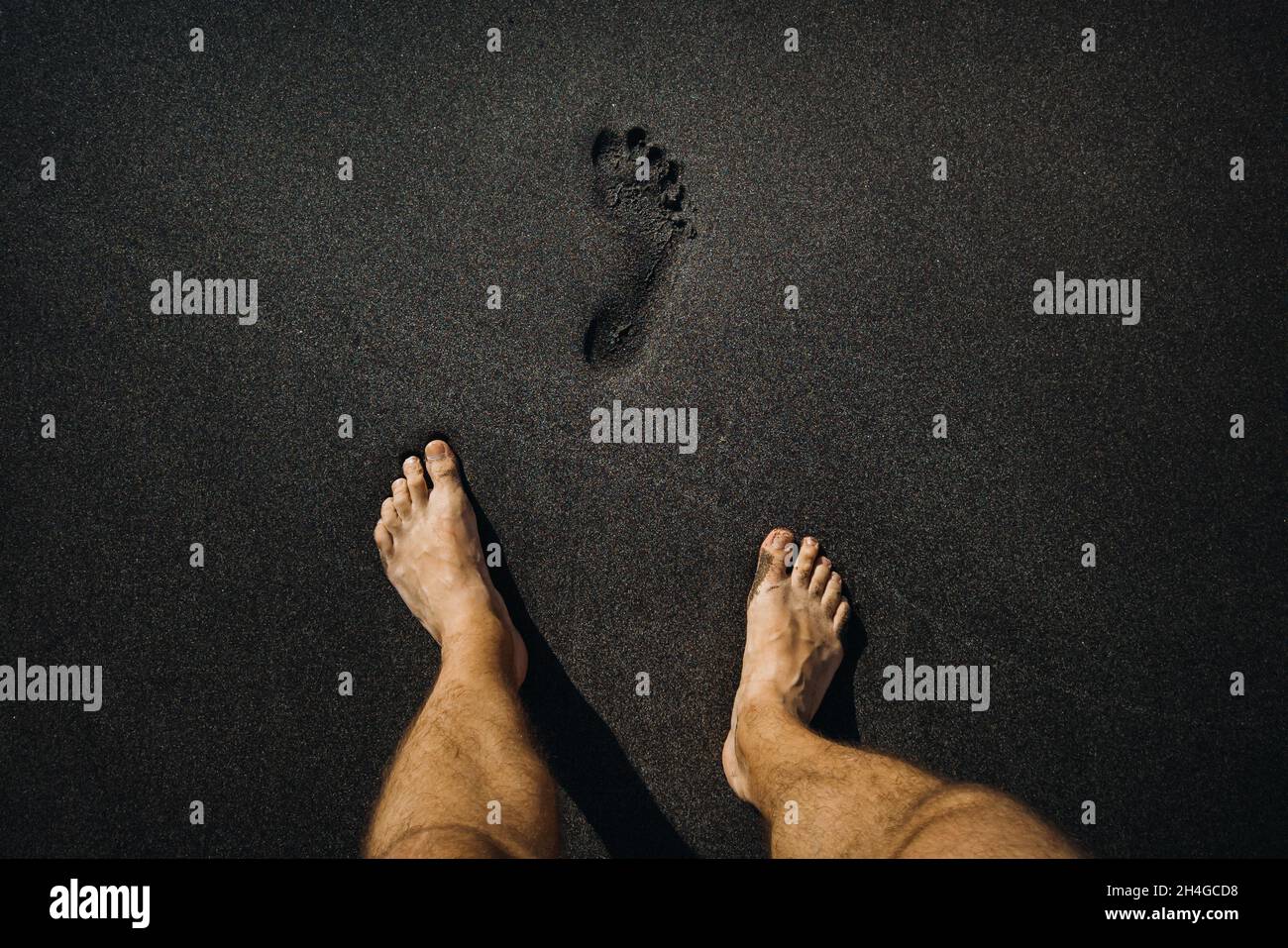 Close up of male footprints and feet walking on the volcanic black sand ...