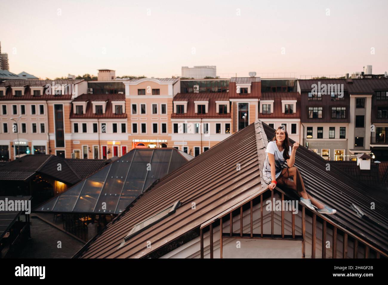 A girl sits on the roof of a house in the city in the evening. Portrait ...