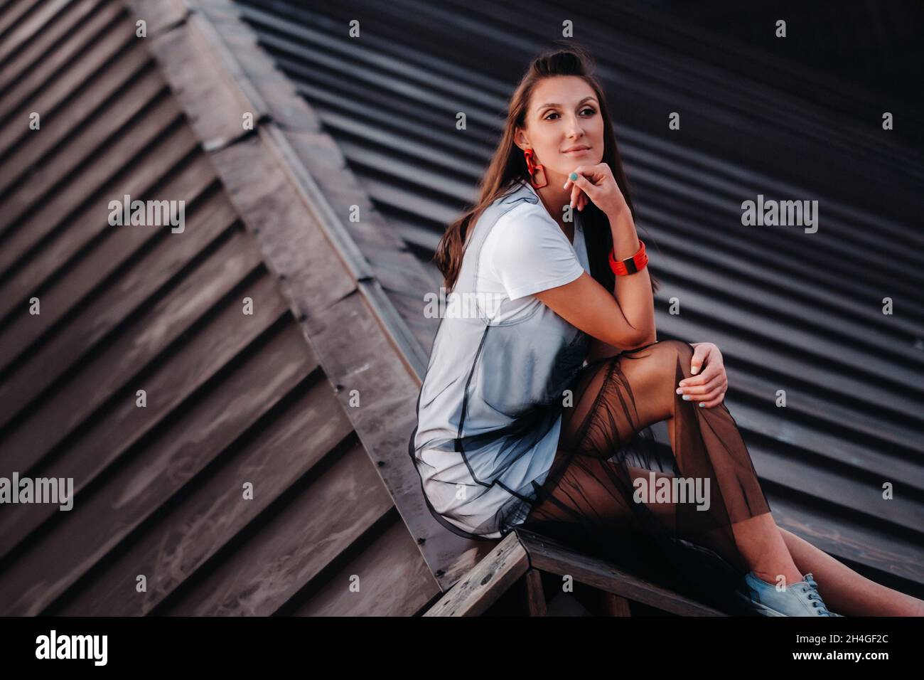 A girl sits on the roof of a house in the city in the evening. Portrait ...