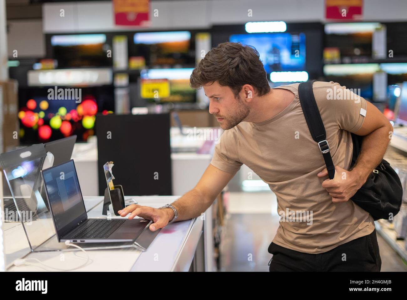 Focused casual man at counter with displayed new laptop checking ...