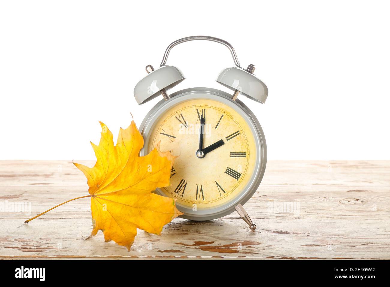 Alarm clock and autumn leaf on table against white background. Daylight ...