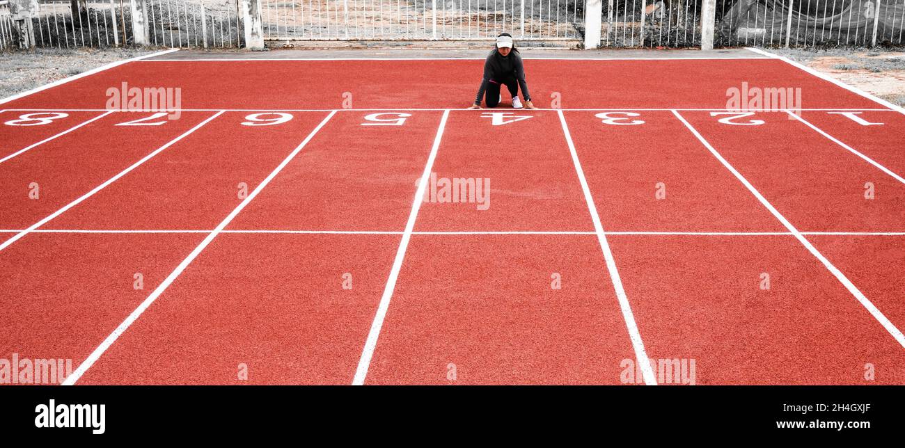 Athletic woman in sport clothes on starting line prepares to run at the ...