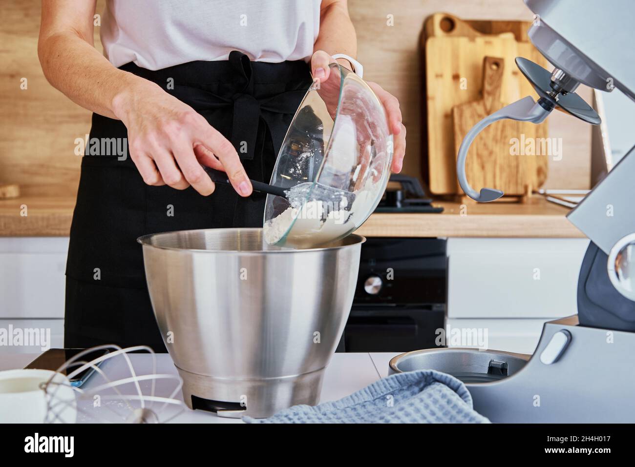 Woman prepares dough using kitchen mixer, pouring ingredients into ...