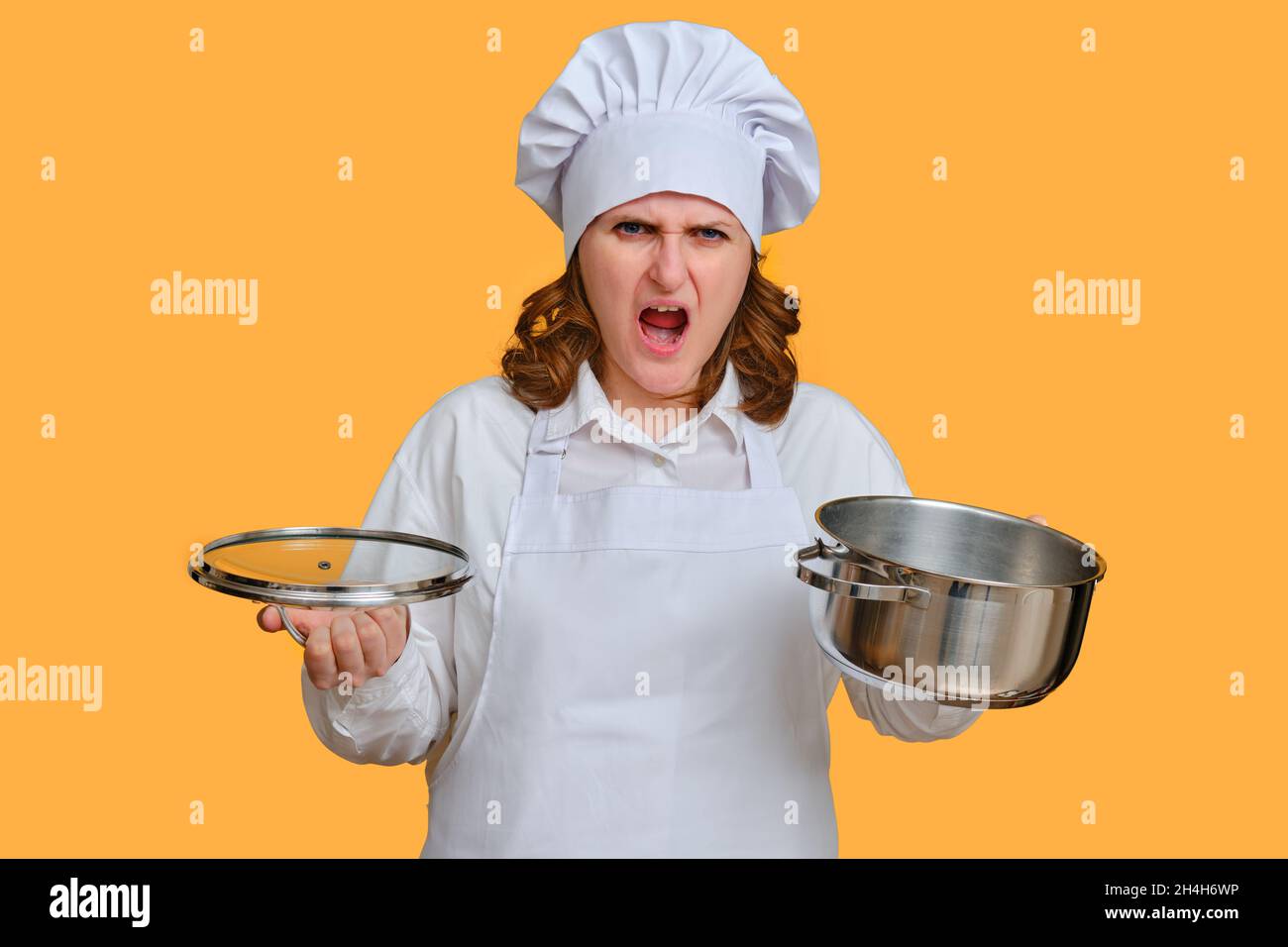 Angry woman chef with a saucepan in her hands yells on a yellow studio ...
