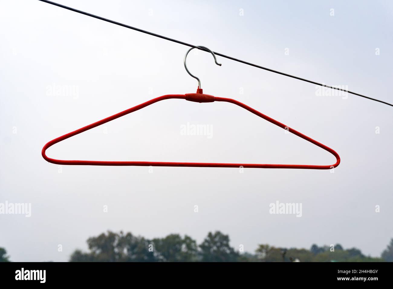 An empty red cloth hanger on the outside with trees in the background ...