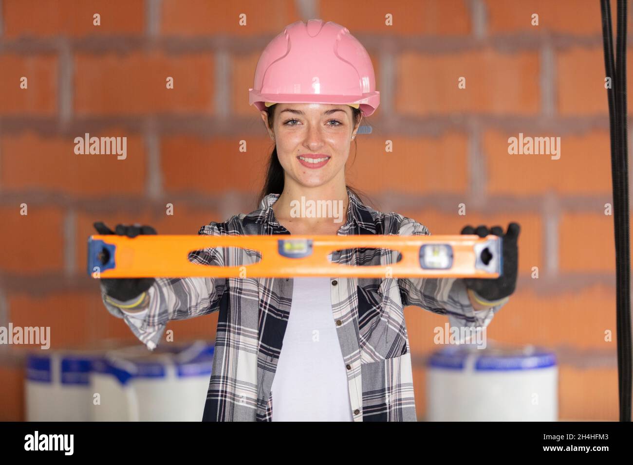 attractive female construction worker in pink hardhat holding spirit ...