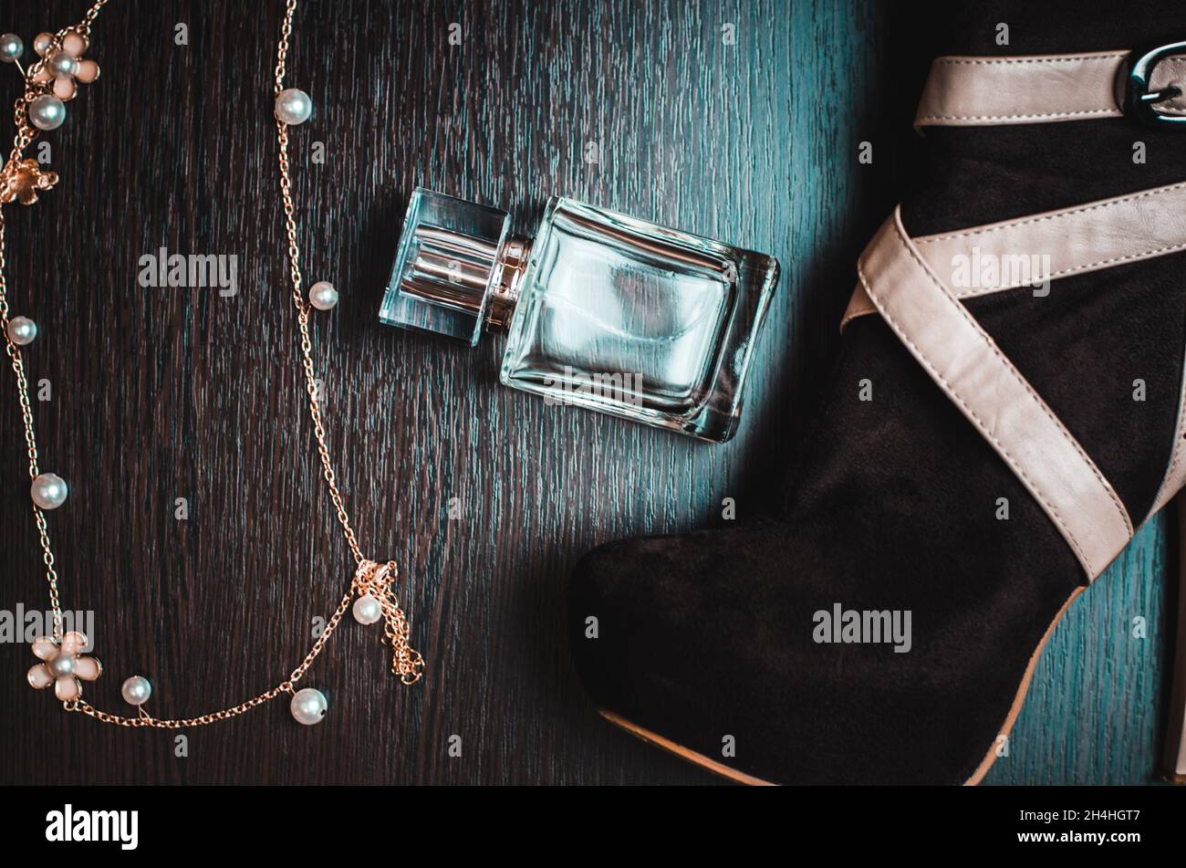 Perfume bottle, women's boots and gold jewelry on wooden background ...