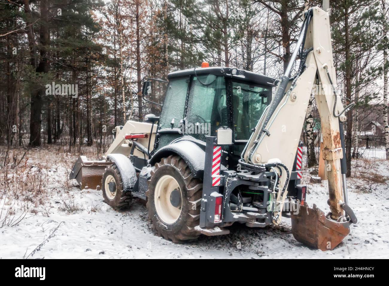 White wheeled tractor excavator on the snow near the forest in winter ...
