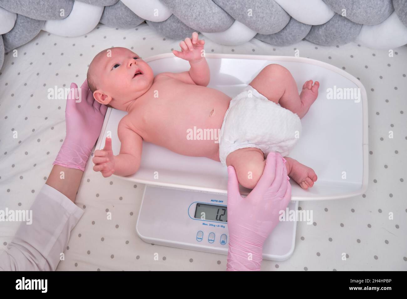 The doctor weighs a newborn baby on a scale. Uniformed nurse taking ...
