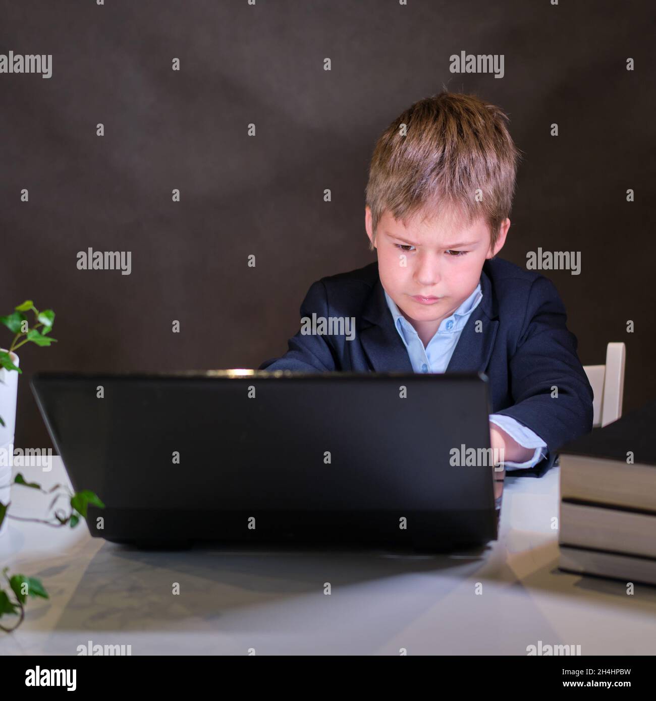 A boy in a school uniform at a computer, copy space on a black studio ...